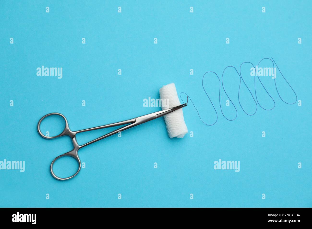 Forceps with suture thread and bandage roll on light blue background ...