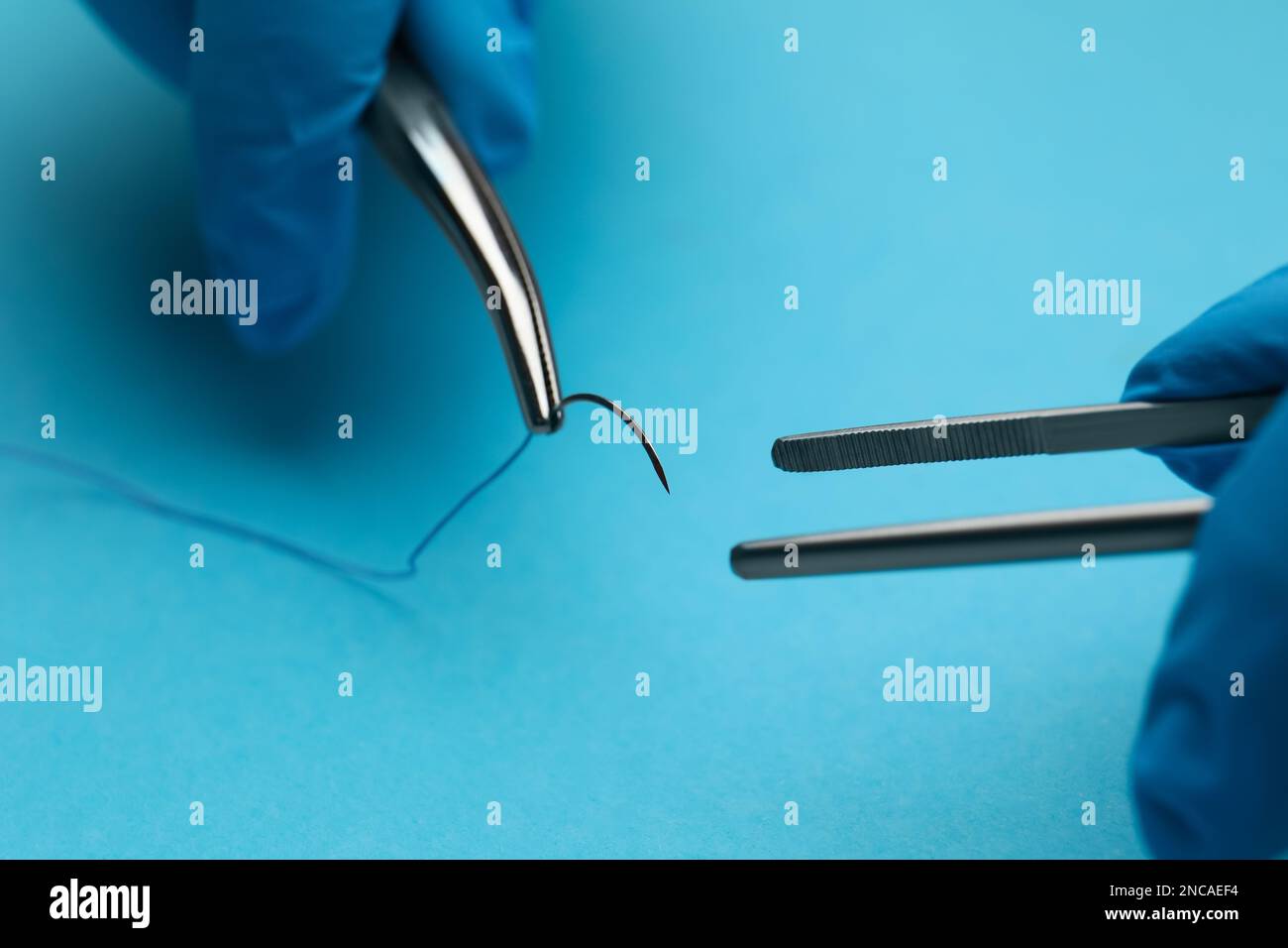 Professional surgeon holding forceps with suture thread on light blue ...
