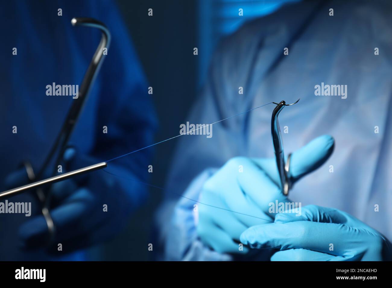 Professional surgeons with forceps and suture thread on blurred ...