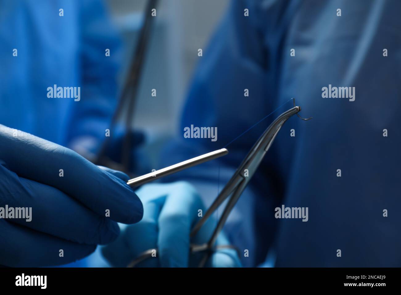 Professional surgeons with forceps and suture thread on blurred ...