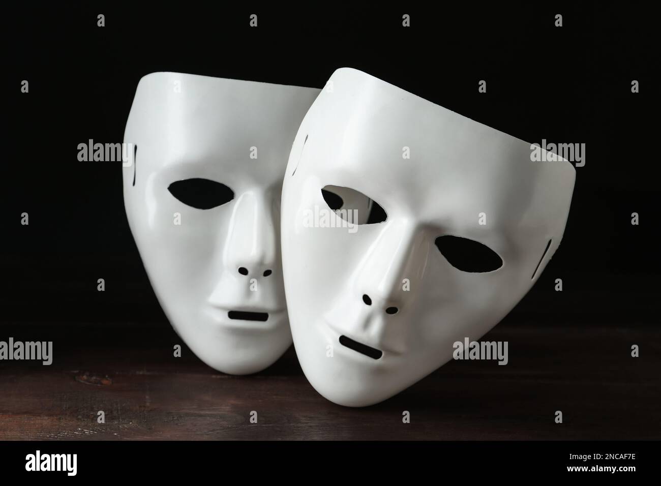 White theatre masks on wooden table against black background Stock ...