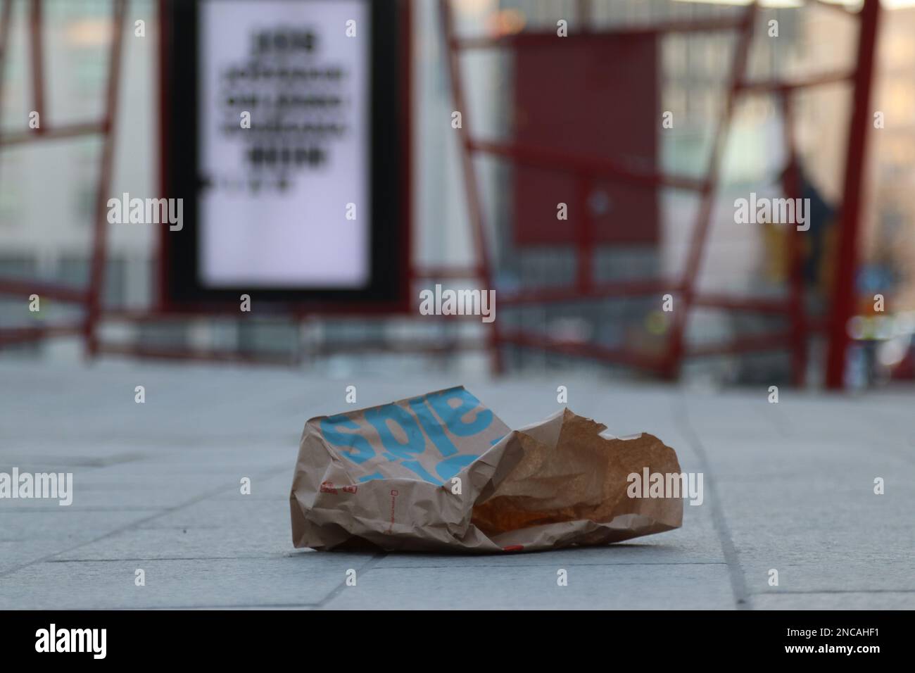 fast food paper bag as garbage in the street with a bus stop background ...
