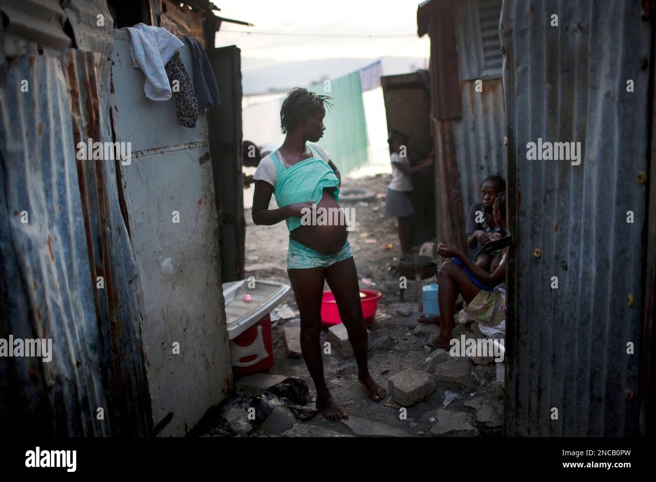 A pregnant woman stands in an alleyway next to shacks at the slum of ...