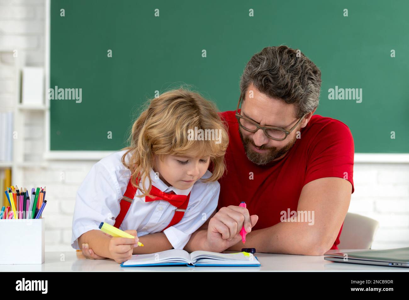 Teacher helping child student pupil from elementary school in classroom ...