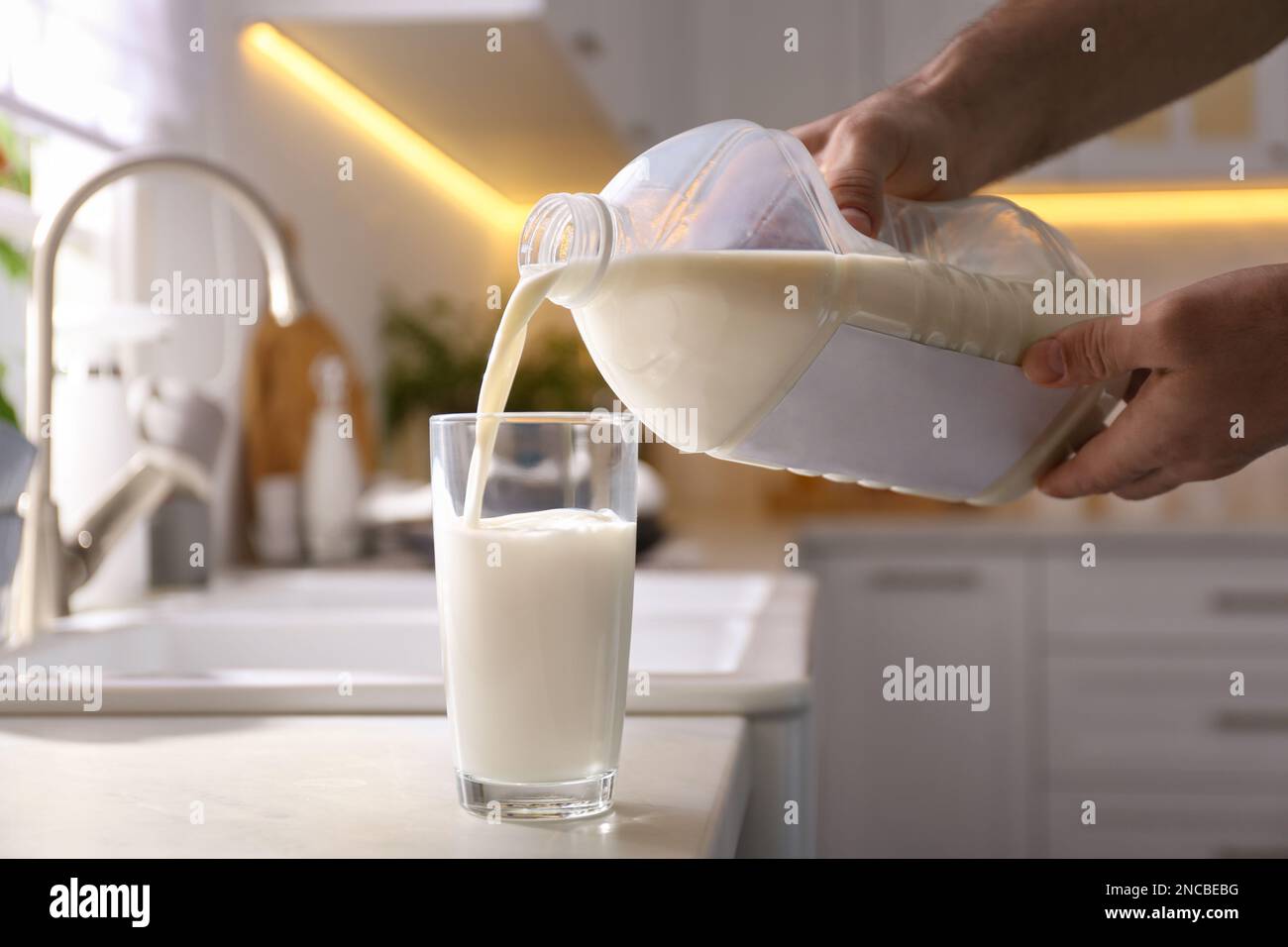 Man pouring milk from gallon bottle into glass at white countertop in ...