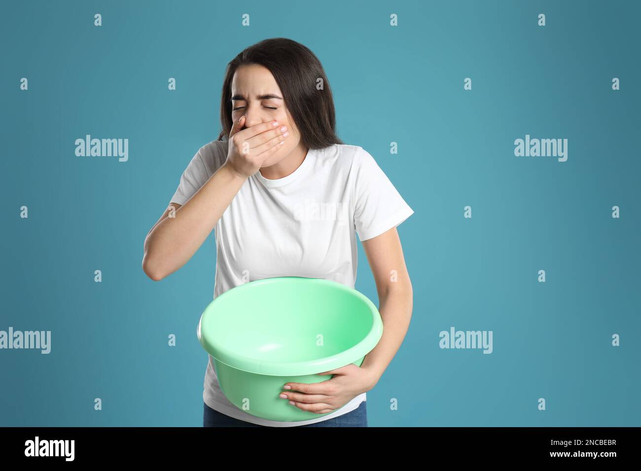 Young woman with basin suffering from nausea on light blue background ...