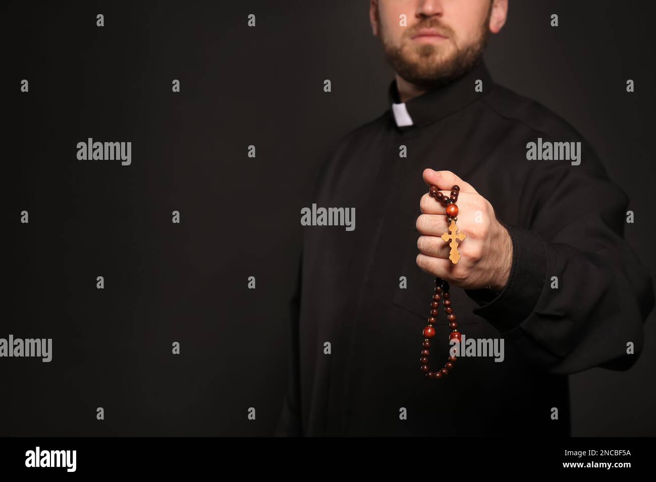 Priest with rosary beads on black background, closeup. Space for text ...