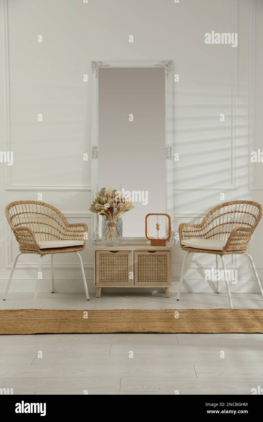 Living room interior with wooden commode, mirror and wicker chairs ...