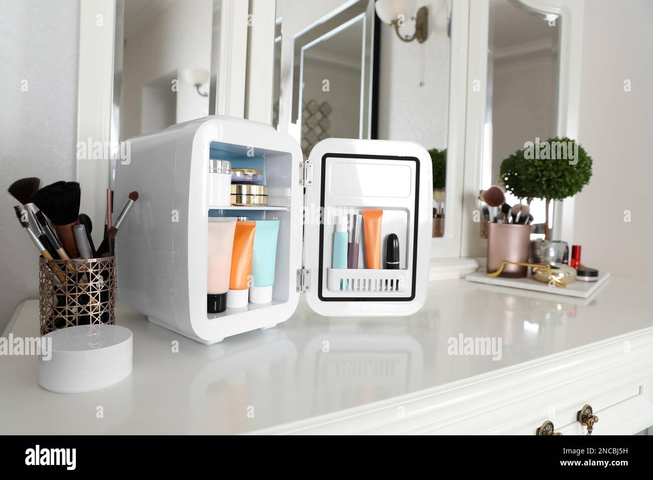 Mini fridge with cosmetic products on white vanity table Stock Photo ...