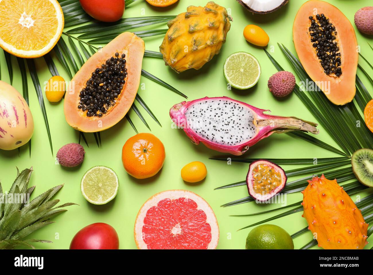 Different exotic fruits and palm leaves on green background, flat lay ...