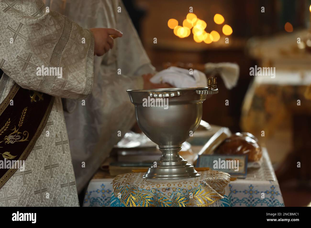 Priests preparing for baptism ceremony. Silver vessel with holy water ...