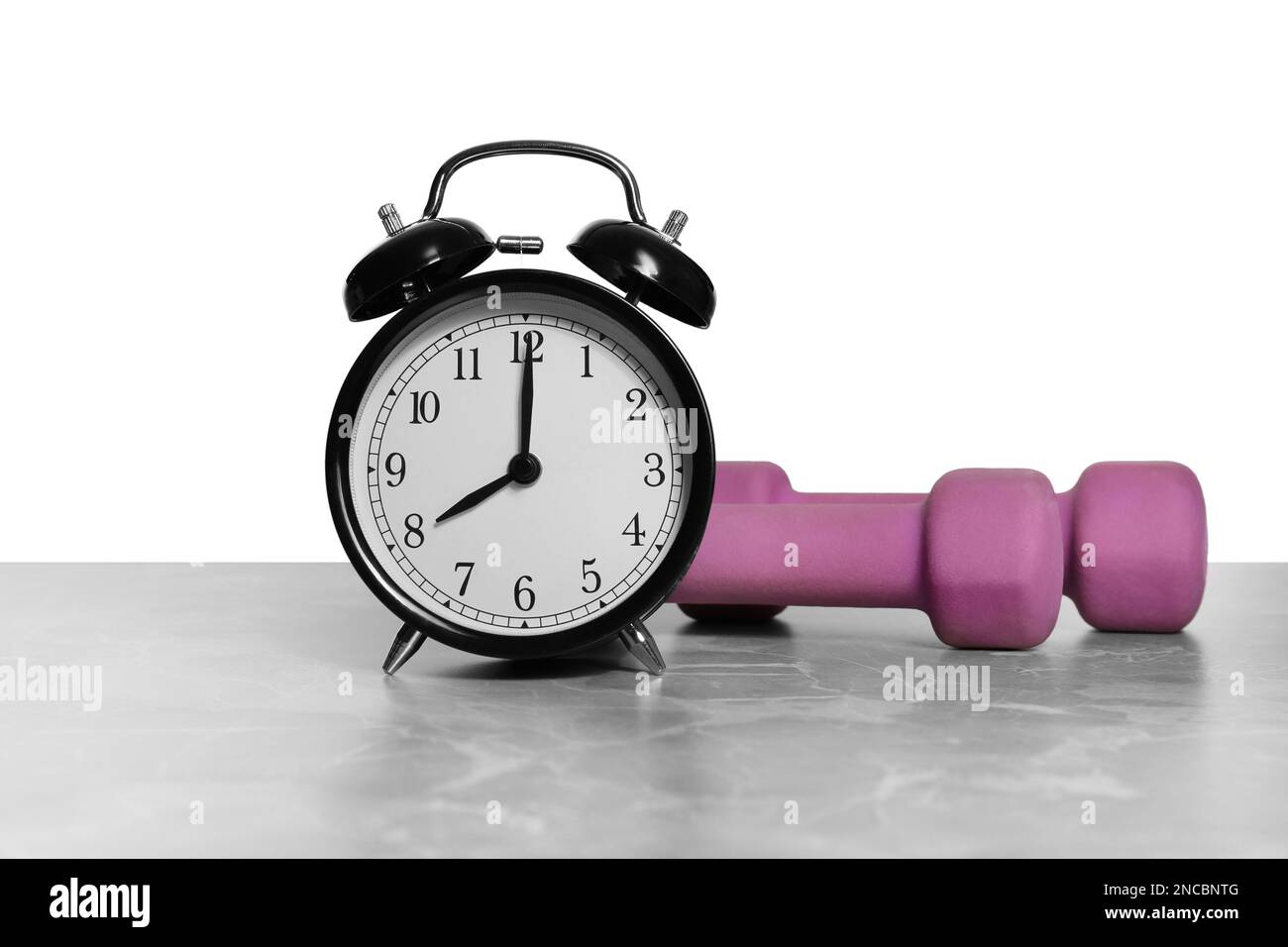 Alarm clock and dumbbells on marble table against grey background ...