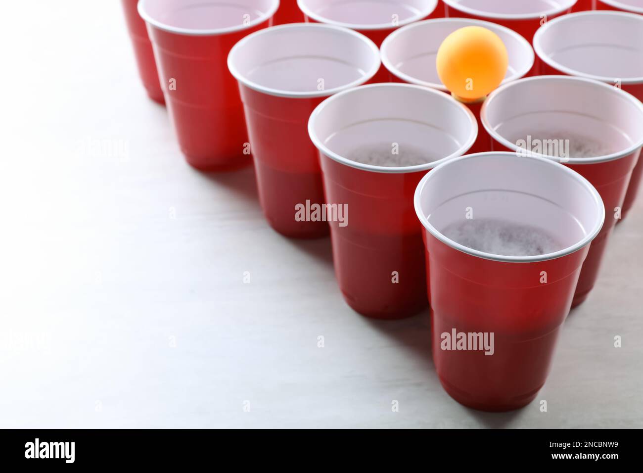 Plastic cups and ball on white table, space for text. Beer pong game ...