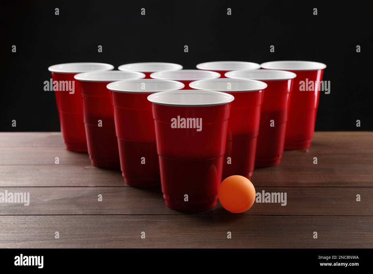 Plastic cups and ball for beer pong on wooden table against black ...