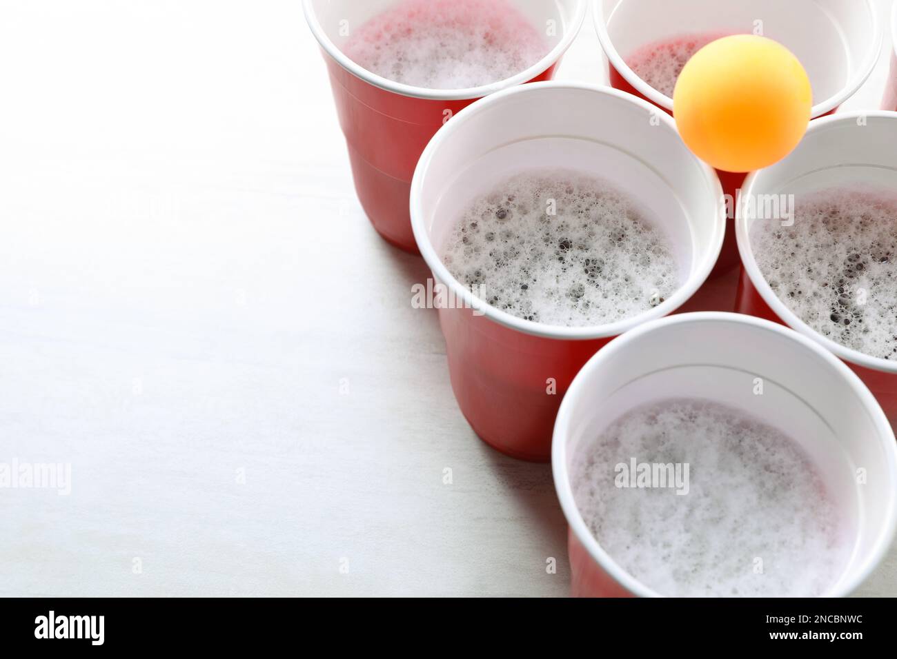 Plastic cups and ball on white table, space for text. Beer pong game ...