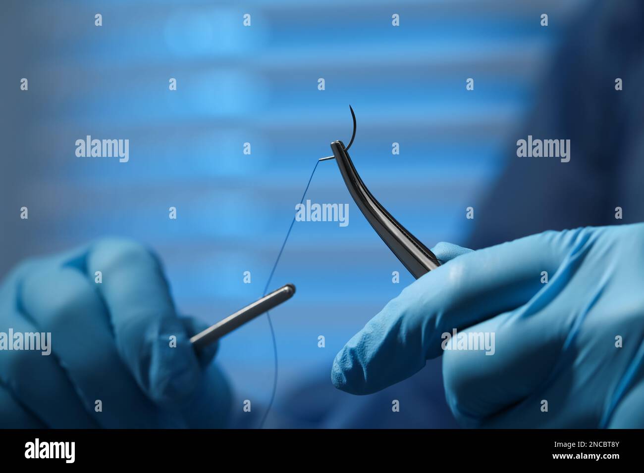 Professional surgeon holding forceps with suture thread on blurred ...