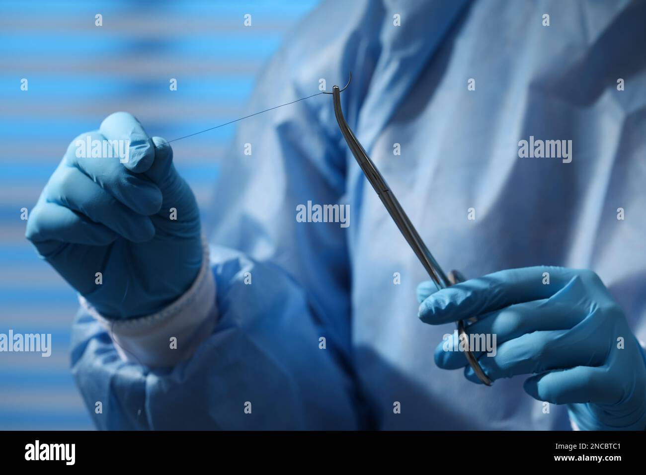 Professional surgeon holding forceps with suture thread on blurred ...
