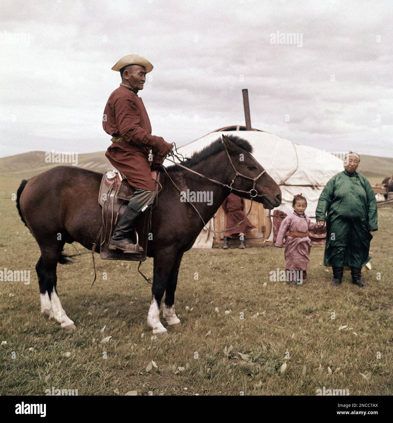A Mongolian herdsman on horseback with his family in front of a yurt, a ...
