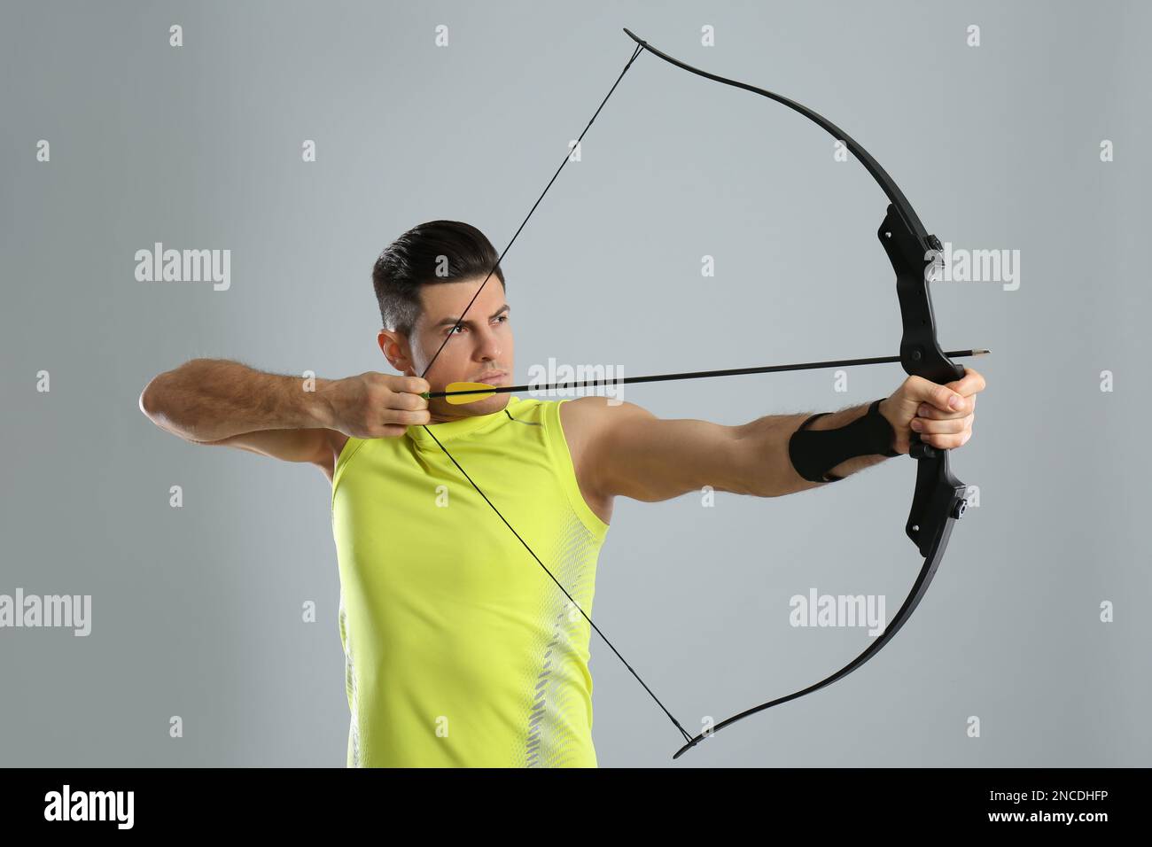 Man with bow and arrow practicing archery on light grey background ...
