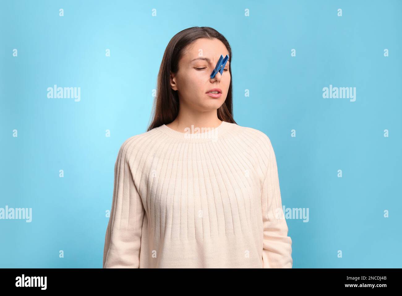 Young woman with clothespin on light blue background. Runny nose ...