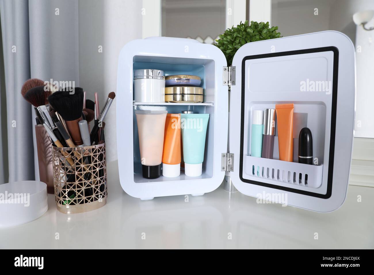 Mini fridge with cosmetic products on white vanity table Stock Photo ...