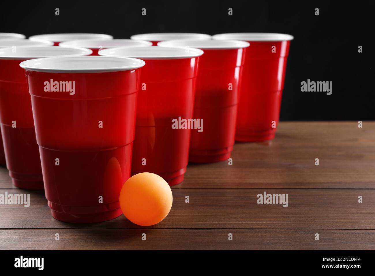 Plastic cups and ball for beer pong on wooden table against black ...