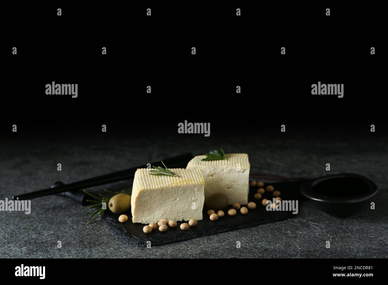 Pieces of delicious tofu with herbs, olives and soy on grey table ...