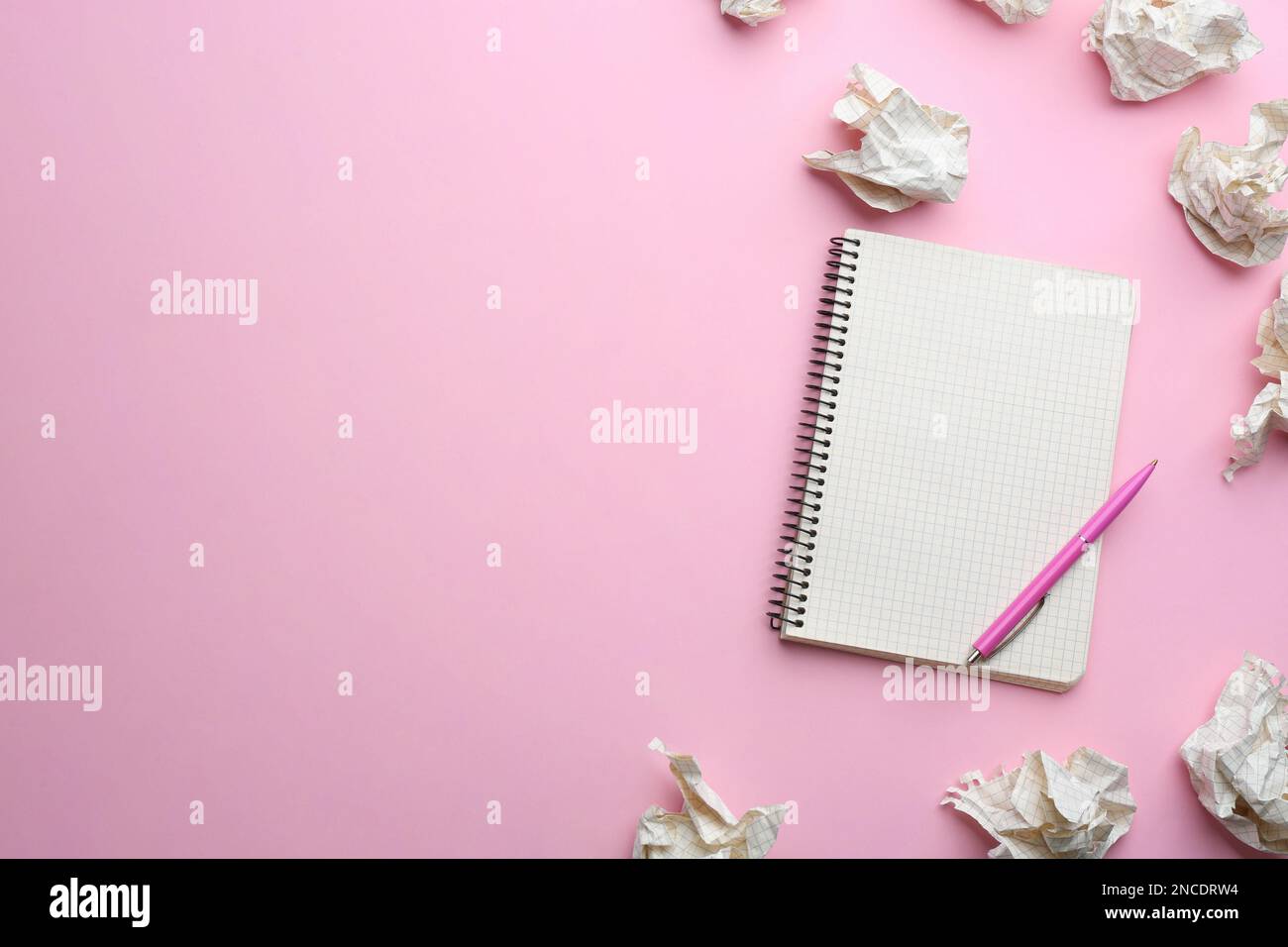 Notebook, pen and crumpled sheets of paper on light pink background ...
