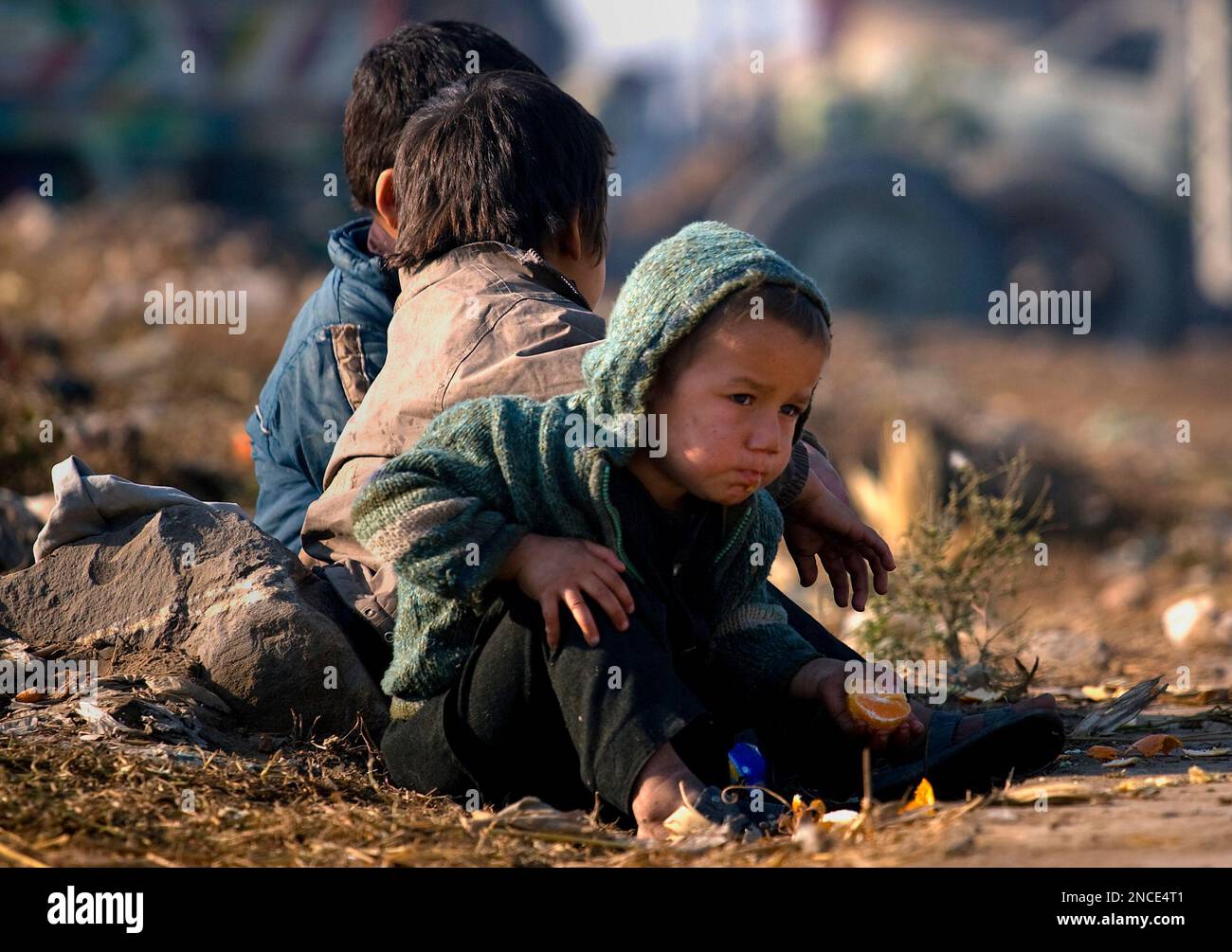 A Pakistani child eats rotting fruit as he sit with his friends next to ...
