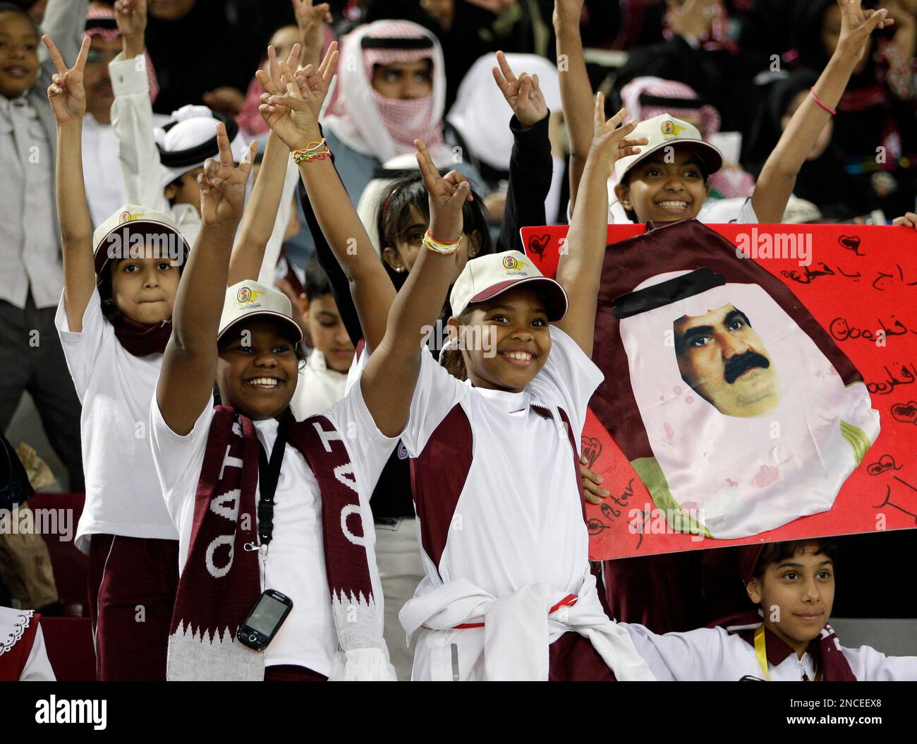 Young Qatari soccer supporters gesture, as they display a poster of ...