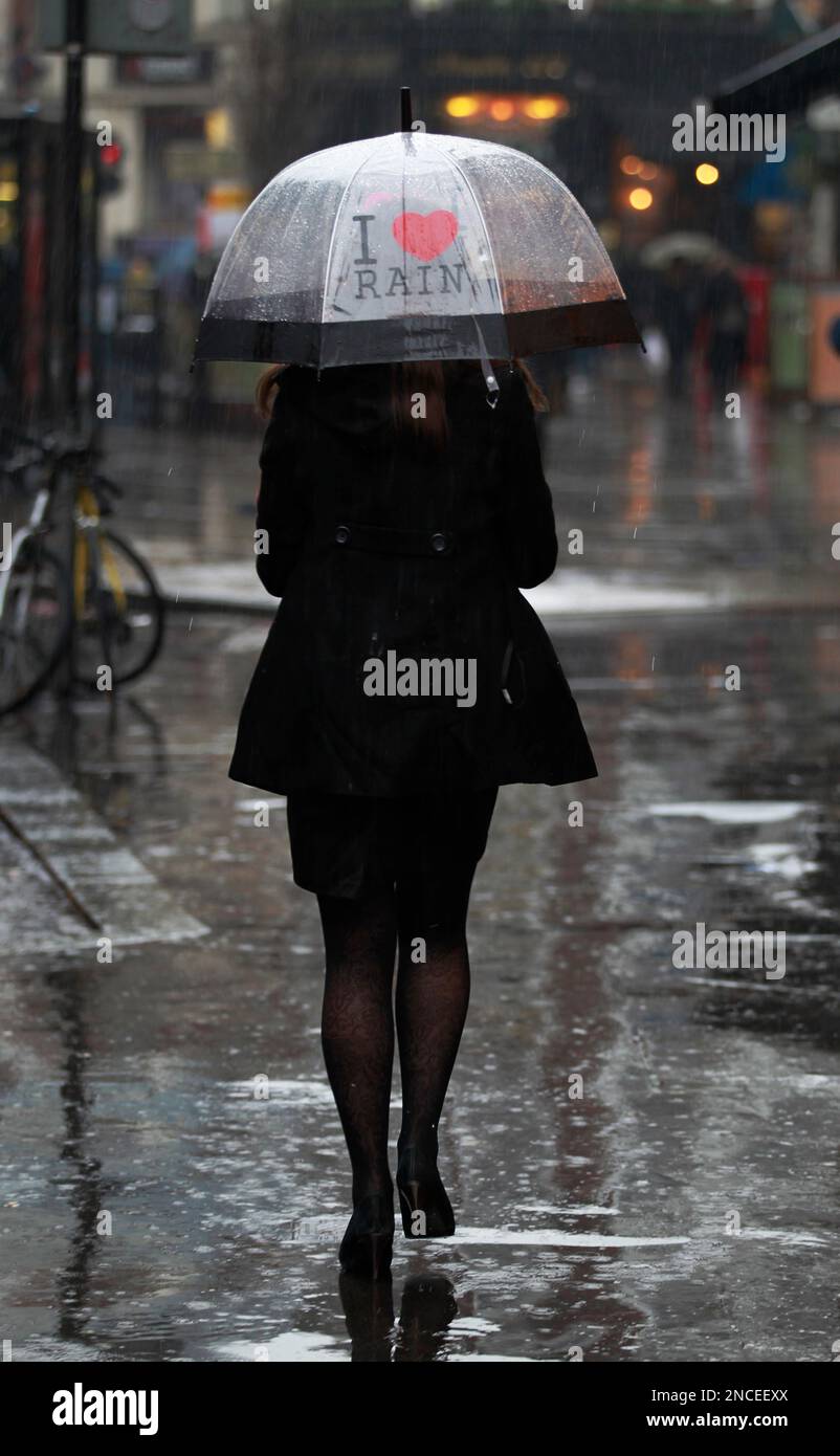 A young woman shelters under an umbrella during a rain shower in London ...