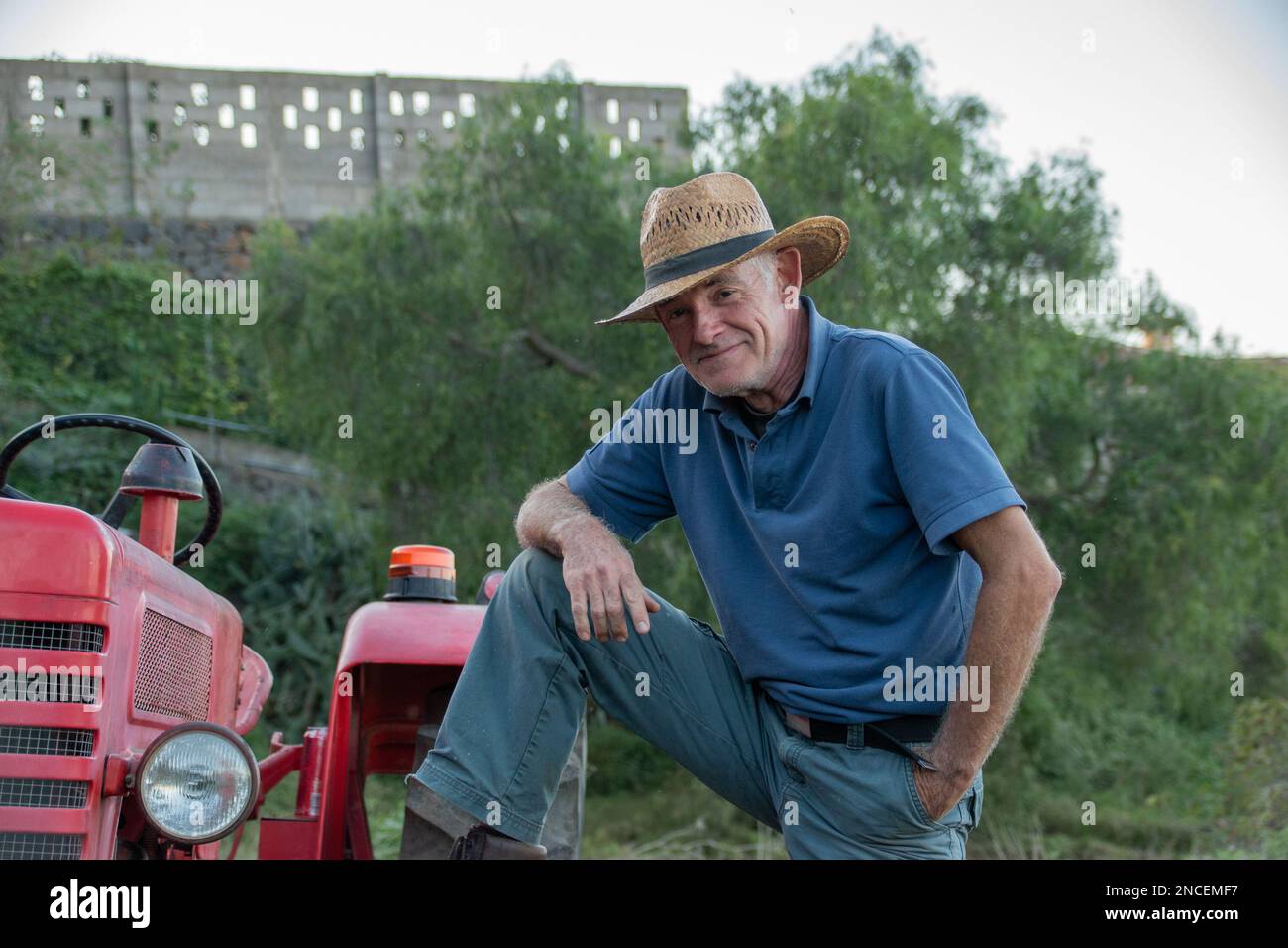 Caucasian farmer leaning on the wheel of his farm tractor. He smiles ...