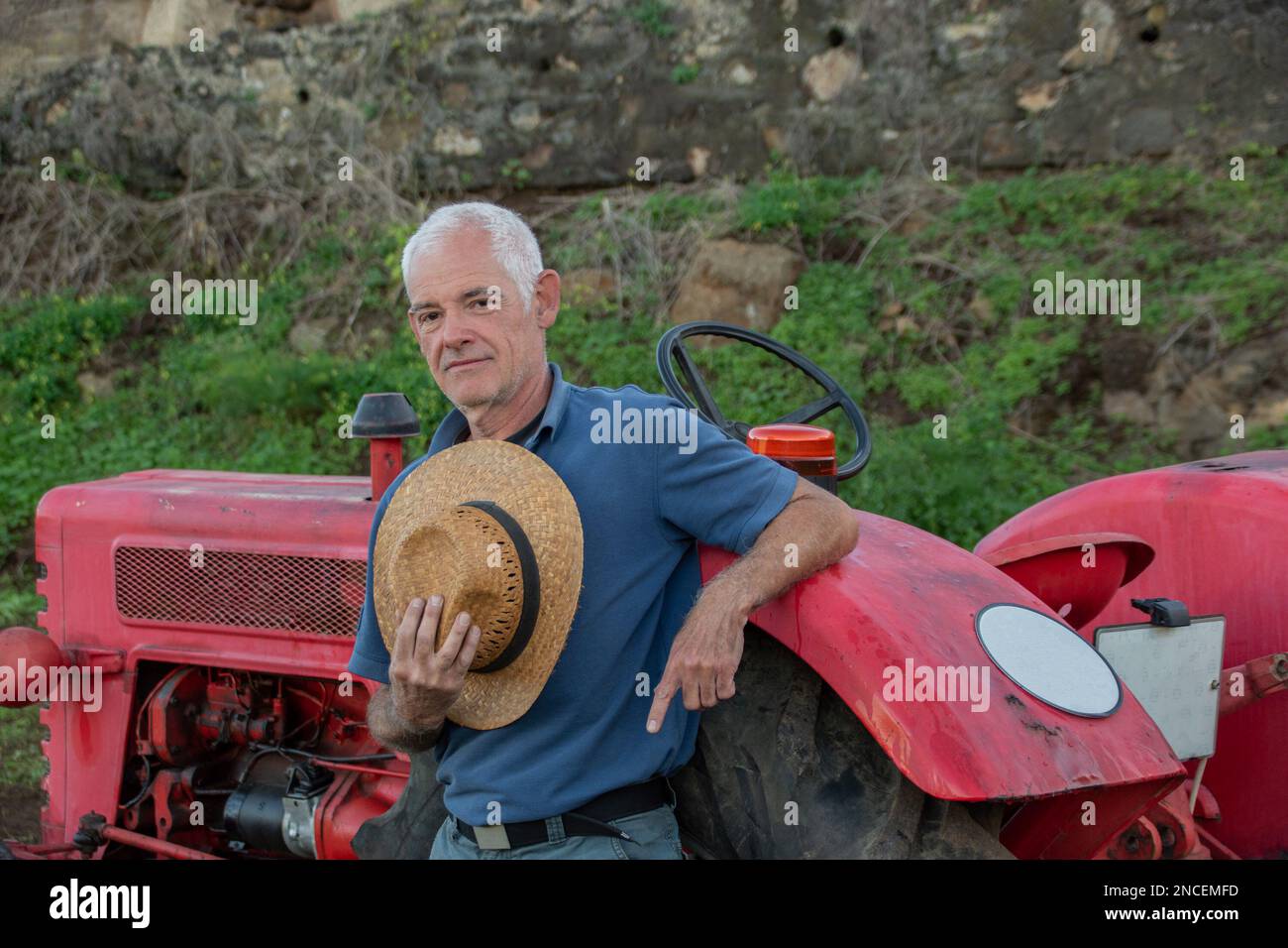 Caucasian farmer with his hat on his chest smiling while leaning on his ...