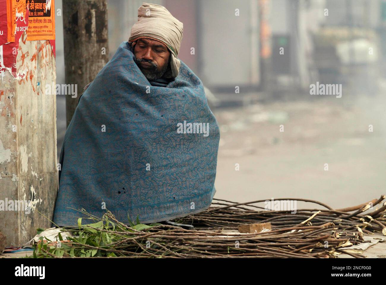 A vendor reacts as he sits wrapped in a blanket in Allahabad, India ...
