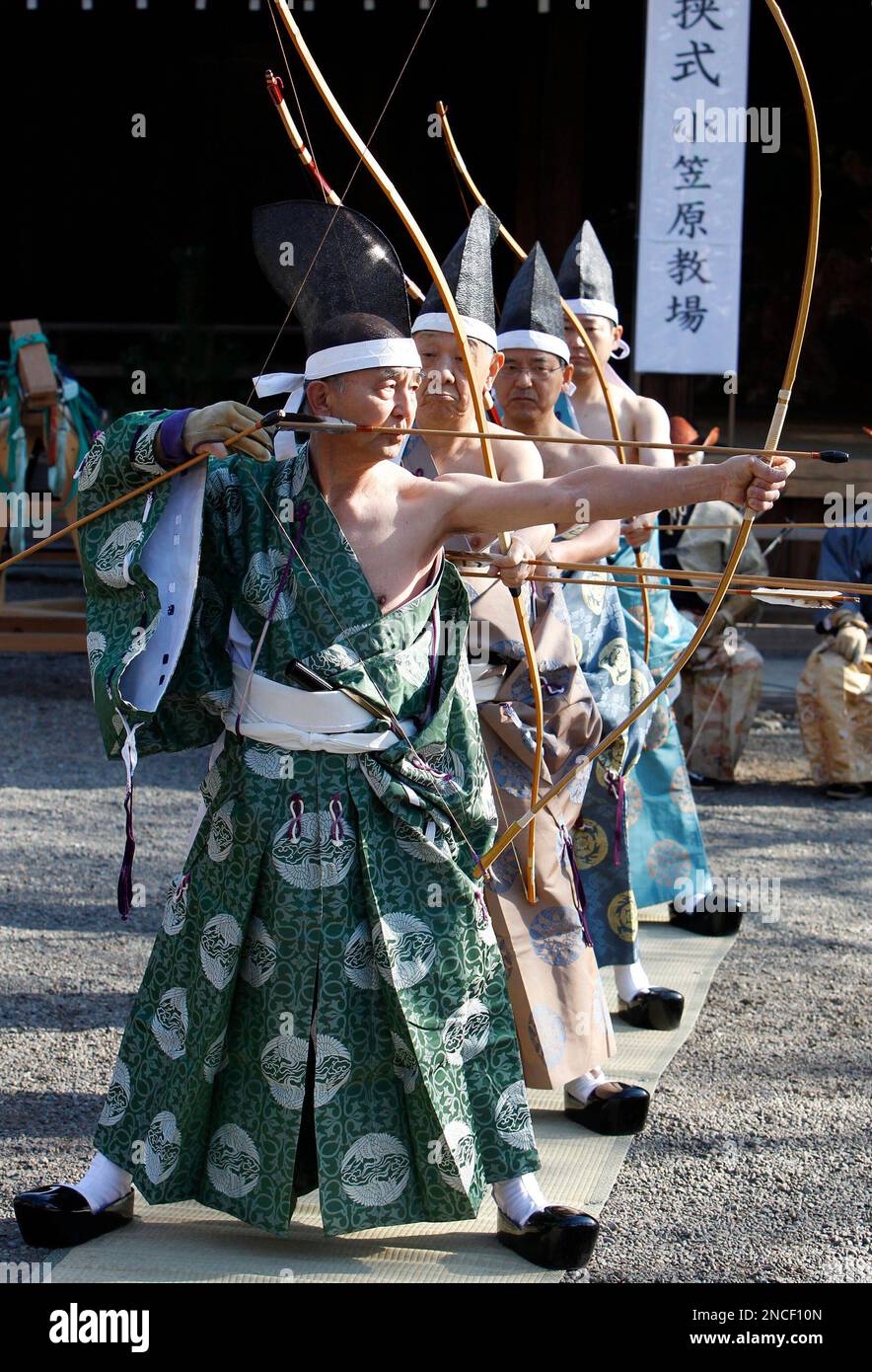 An archer dressed in a traditional Japanese warrior's attire aims an ...