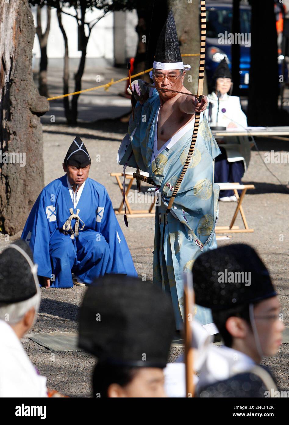 An archer dressed in a traditional Japanese warrior's attire aims an ...