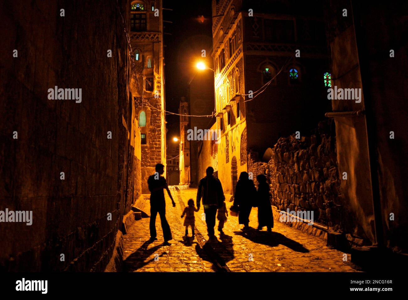 Yemenis walk back to their homes through an alley of the old city of ...