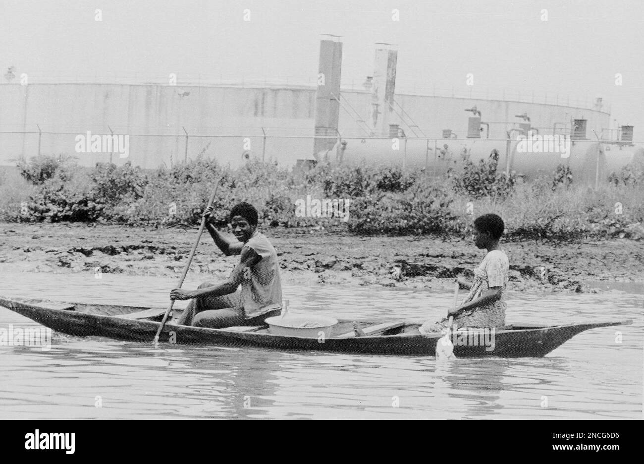 A traditional canoe carries two Nigerians past the tanks of an oil ...