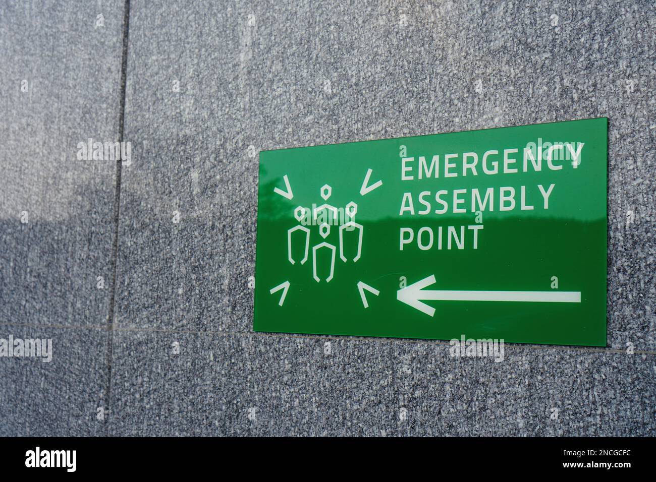 Emergency sssembly point sign on the textured wall. Assemble here for ...