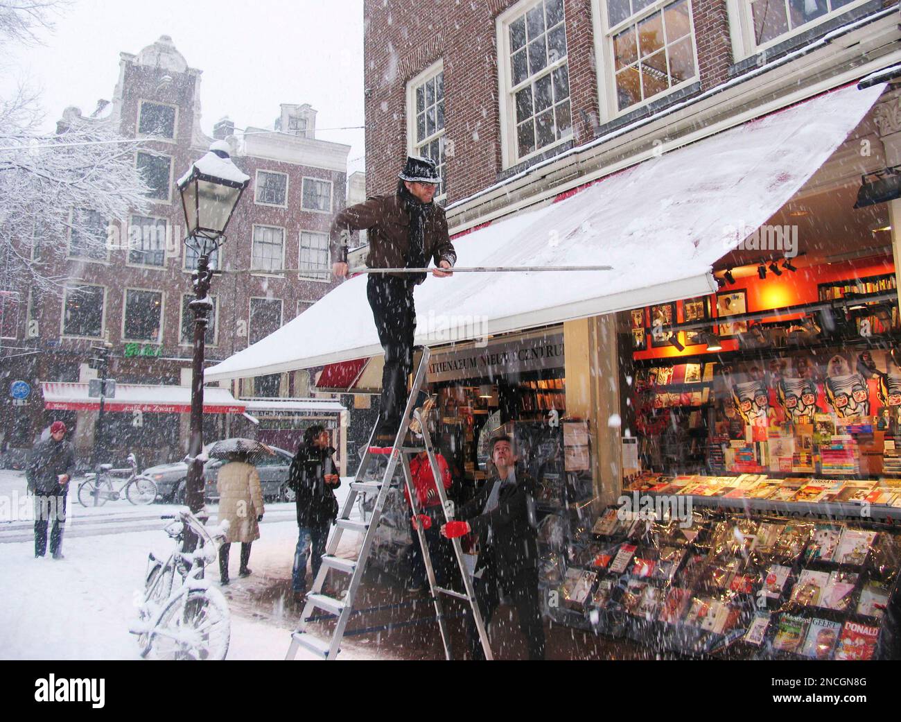 A man removes snow from an awning of a bookstore during snowfall in ...