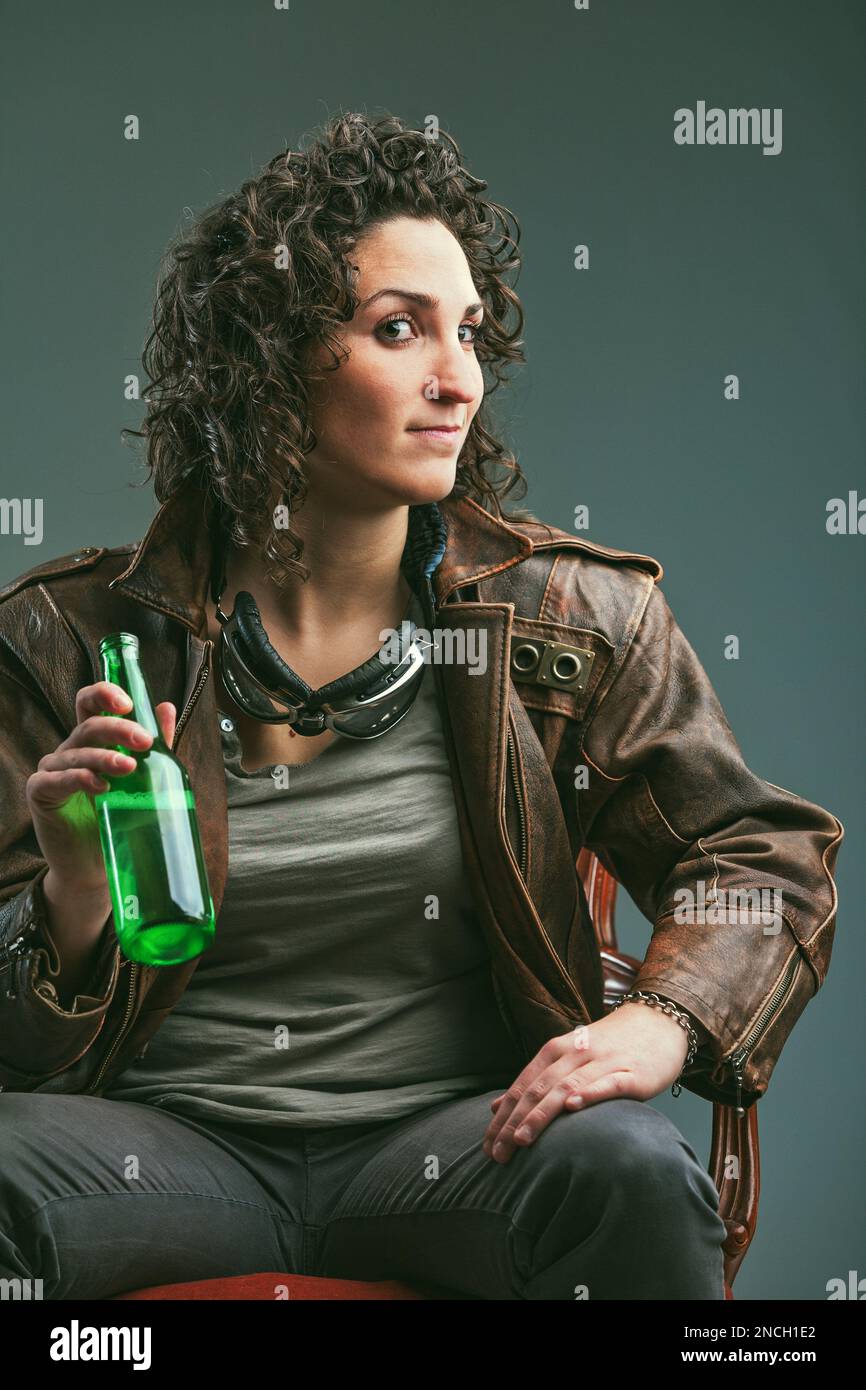 Elegant chair portrait of a biker woman in leather jacket and goggles ...
