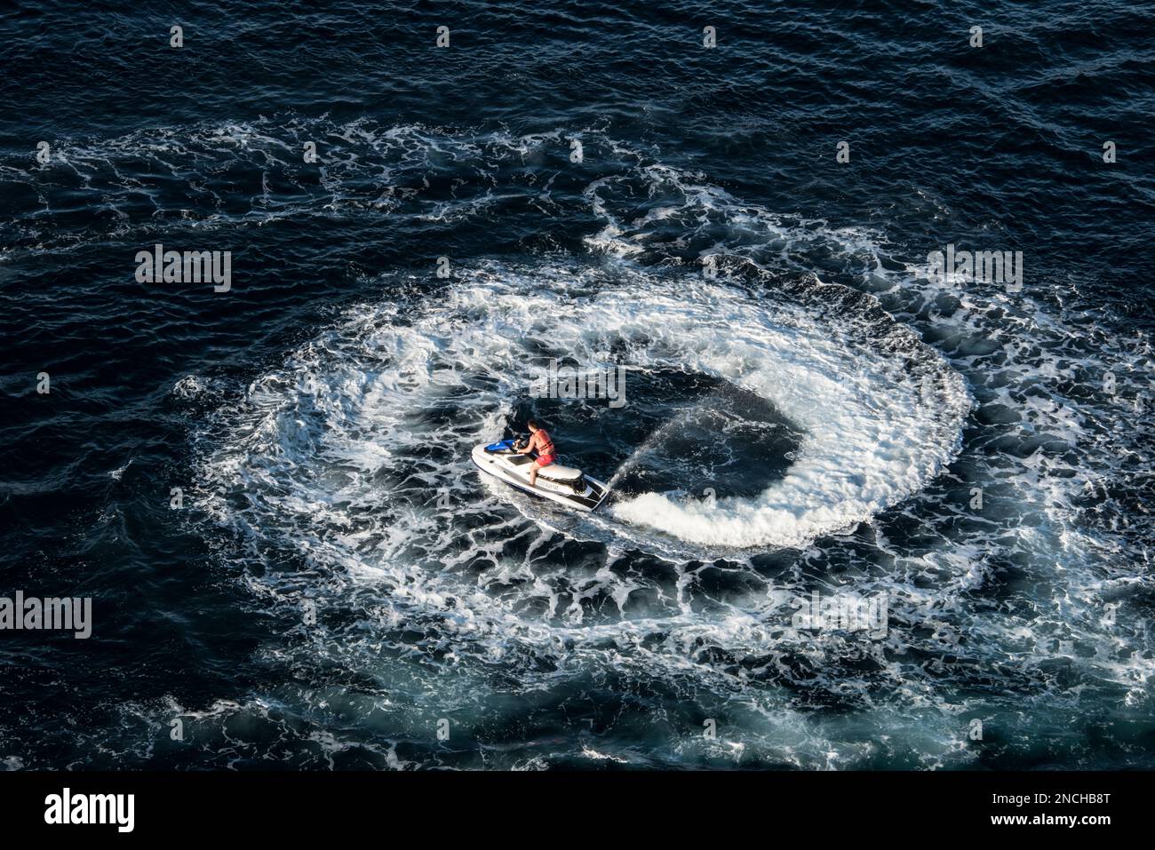 An unidentifiable man rides a personal watercraft, jet ski, creating a ...
