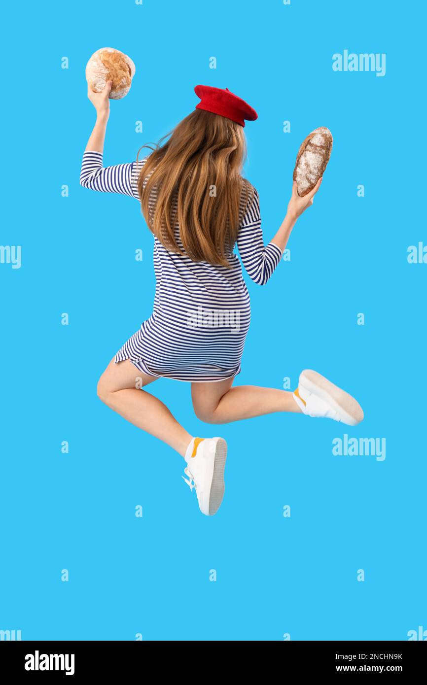 Young woman in beret with loaves of fresh bread jumping on blue ...