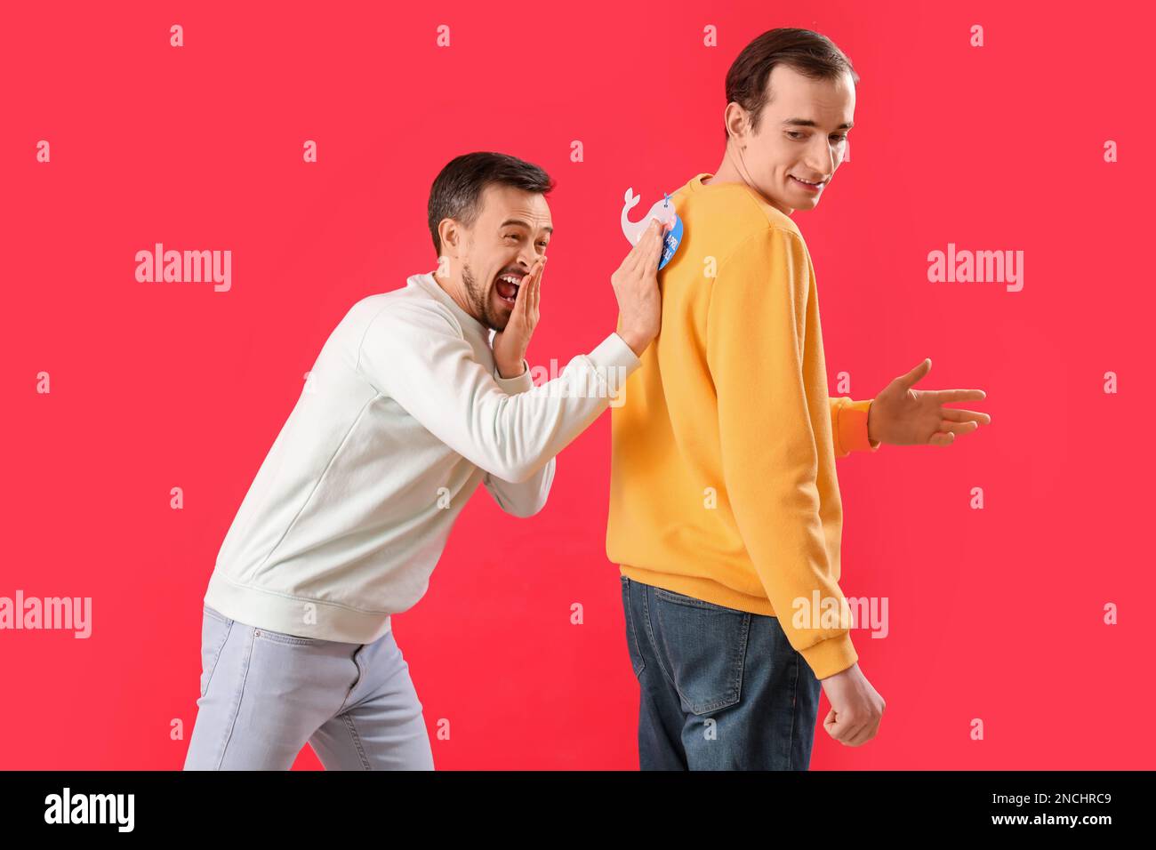 Young man sticking paper on his friend's back against red background ...