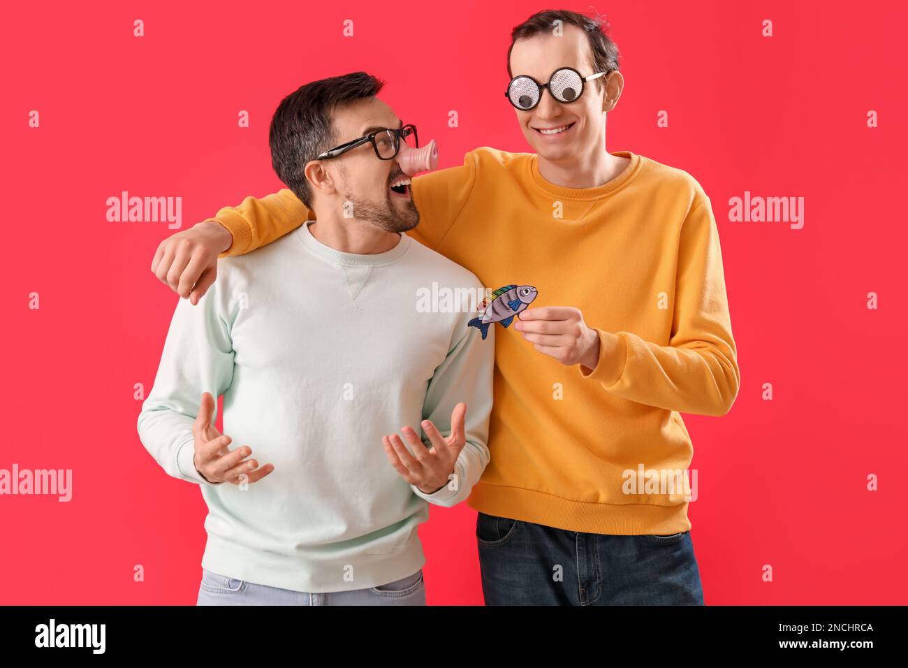 Young men in funny disguise with paper fish on red background. April ...
