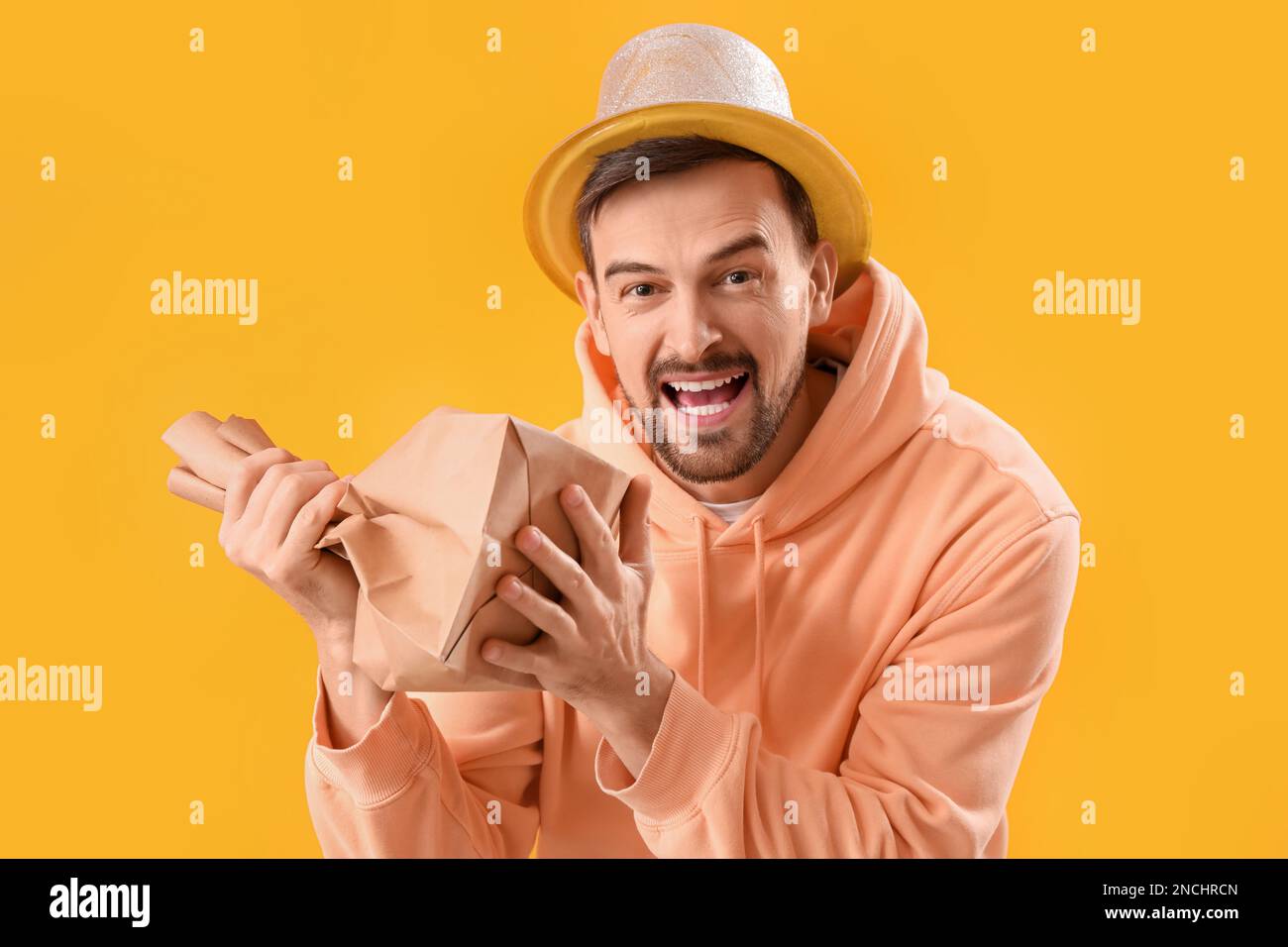 Funny young man with paper bag on yellow background. April Fools' Day ...