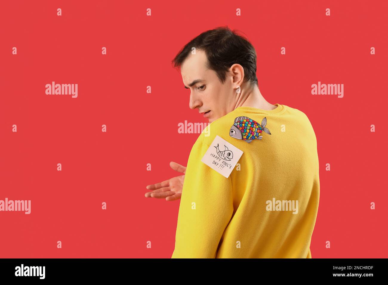 Sticky paper with text HAPPY FOOL'S DAY and fish on young man's back against red background ...