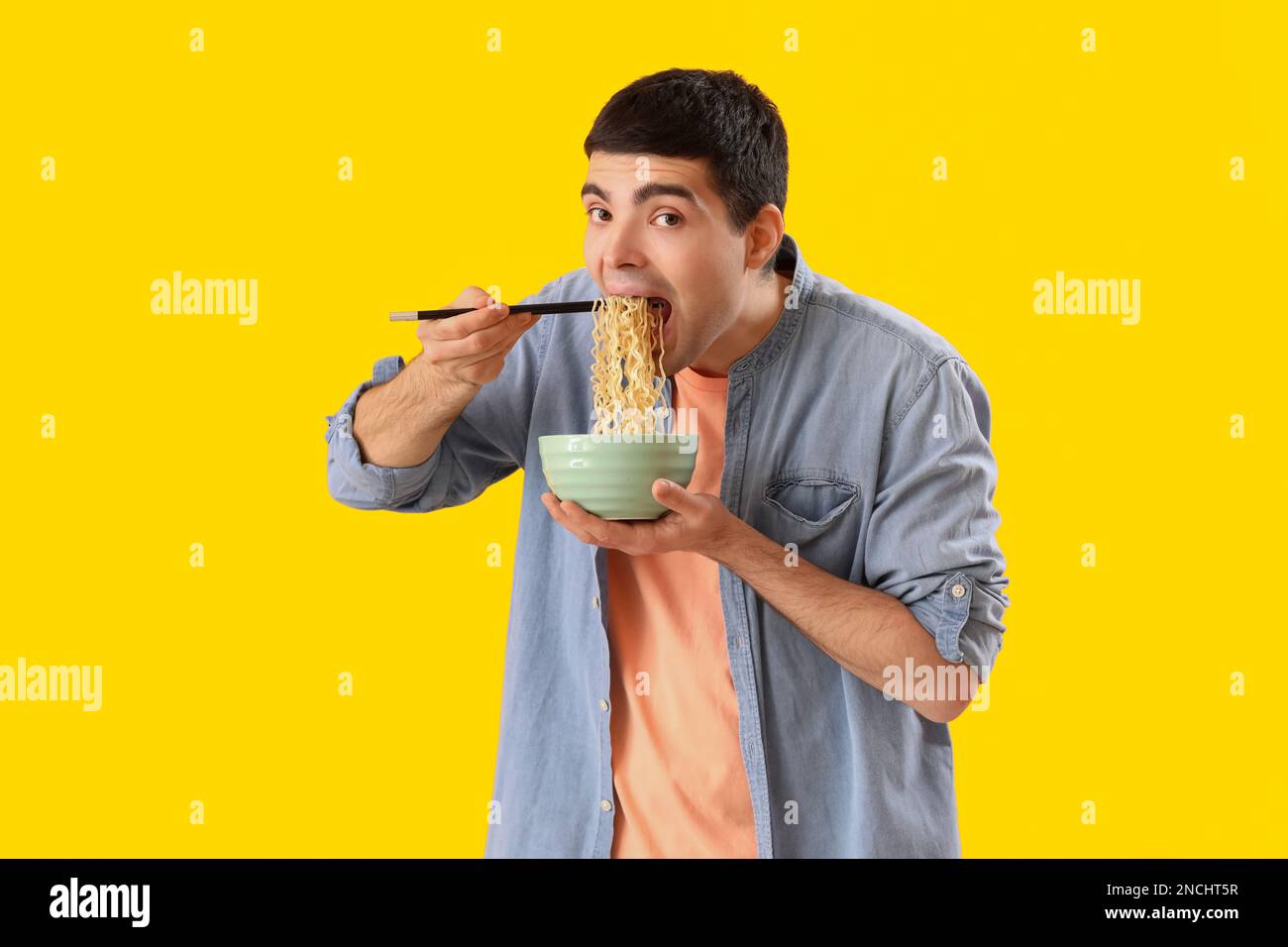 Young man eating Chinese noodles on yellow background Stock Photo - Alamy