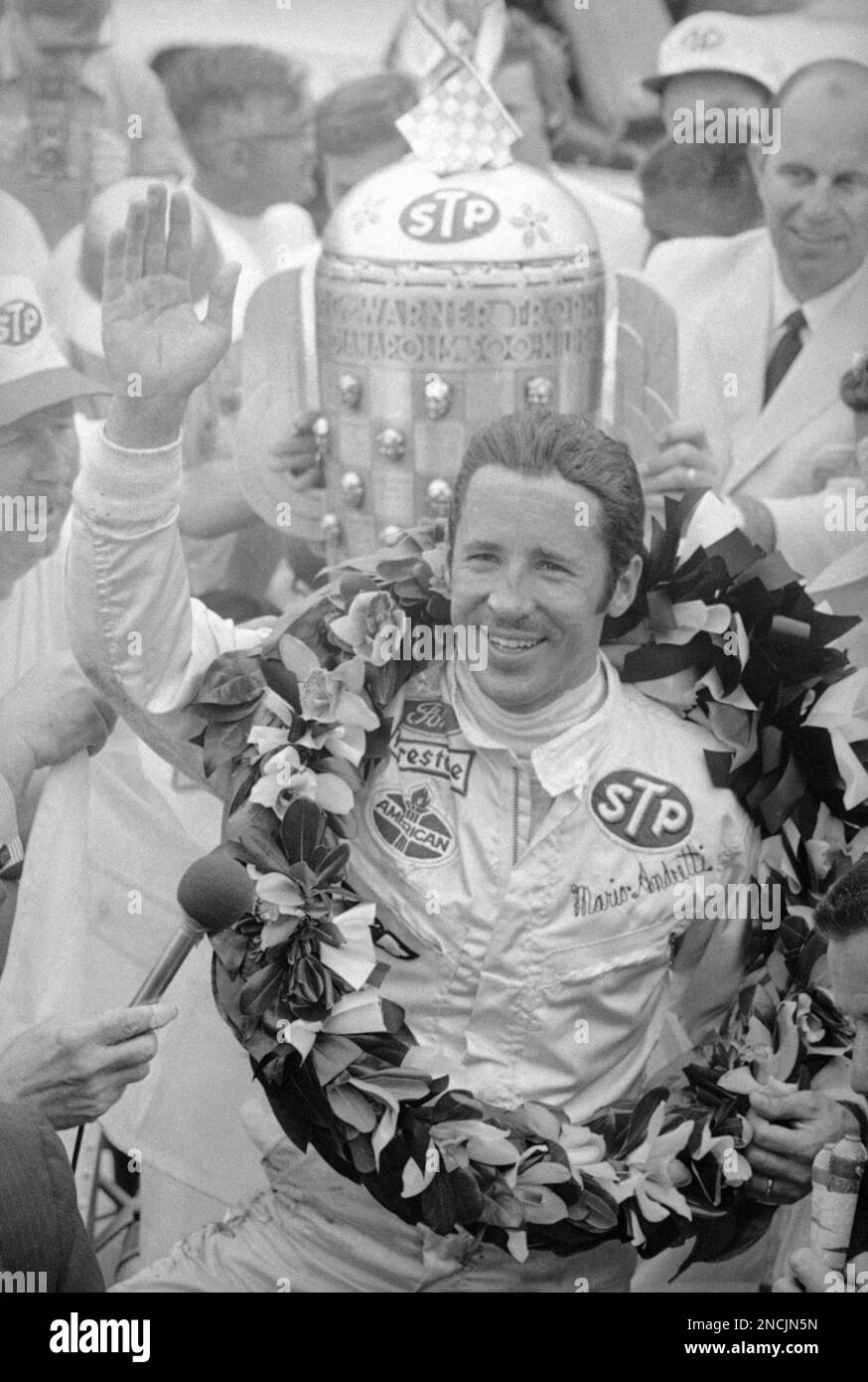 Mario Andretti has a big smile and is wearing a wreath of flowers in ...