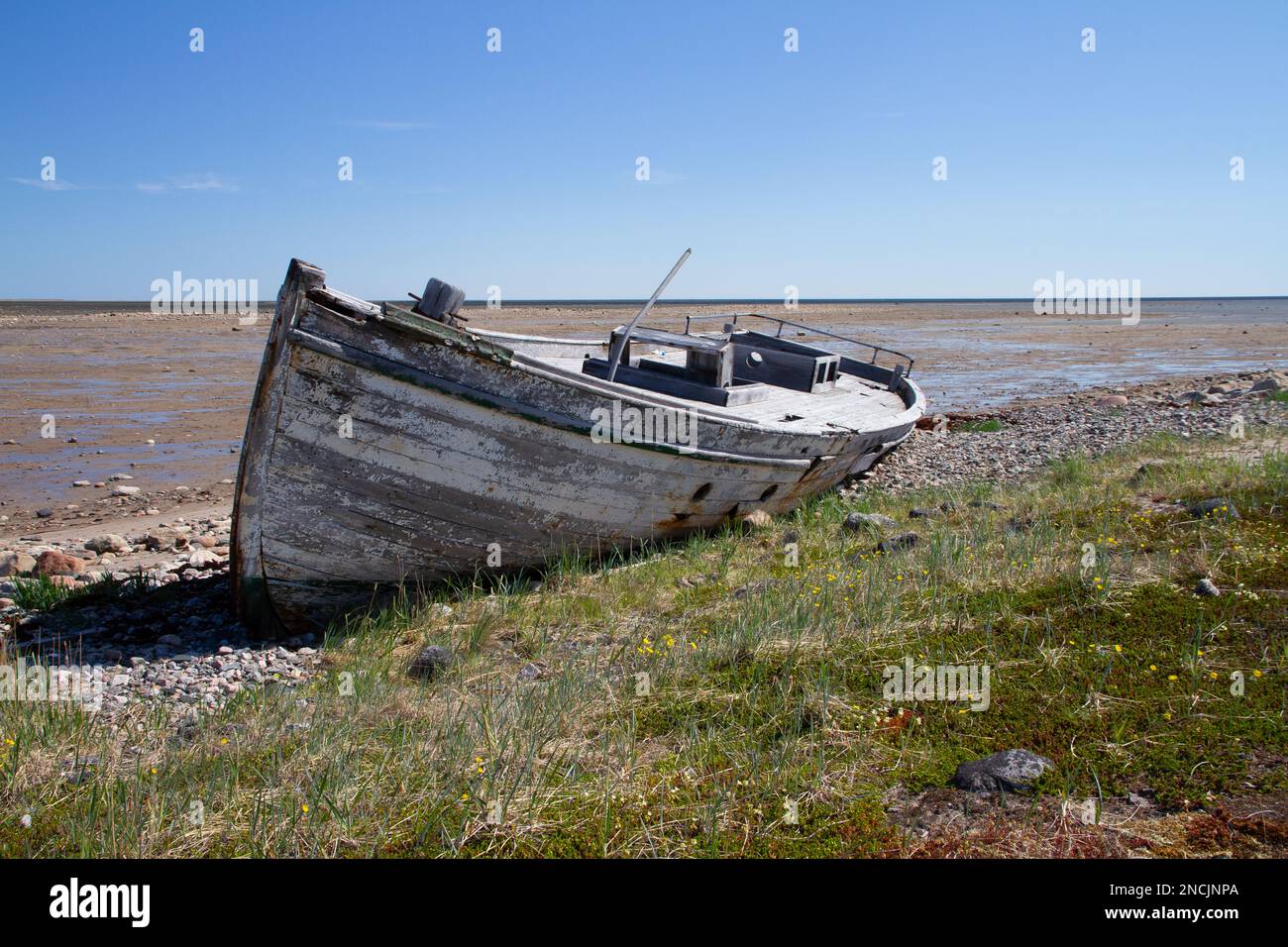 Front view of old wooden boat wrecked and stranded on a rocky shoreline ...